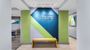 Um lobby moderno com um banco de madeira, design geométrico na parede e uma placa com a frase 'É preciso apenas uma faísca'.