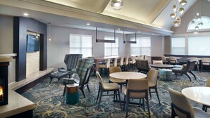 Um hall de hotel com lareira, vários espaços para sentar e luminárias pendentes.