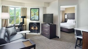 Quarto de hotel com sofá, televisão, lareira, cama e escrivaninha.