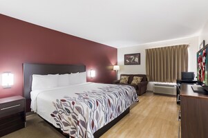Quarto de hotel com cama, mesa de cabeceira, luminária, TV e janela com cortinas.