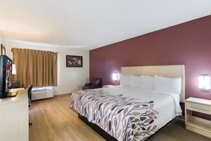 Quarto de hotel com cama, escrivaninha, cadeira, televisão e janela com cortinas.