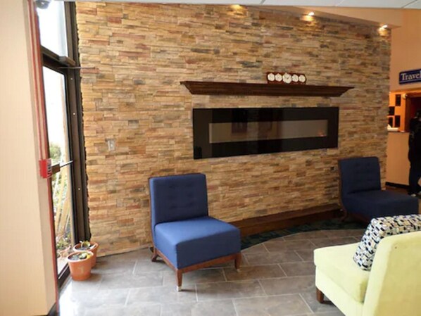 Um lobby com parede de pedra, uma TV de tela plana, duas poltronas azuis e uma poltrona amarela.