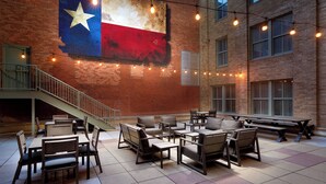Uma área externa com mesas e cadeiras, uma escada e um mural da bandeira do Texas.