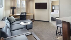 Quarto de hotel com sofá, escrivaninha, televisão de tela plana, cama e mesa pequena.