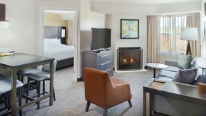 Quarto de hotel com cama, TV, lareira, espaço para refeições e área de estar.