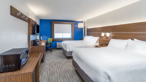 Quarto de hotel com duas camas, uma mesa com micro-ondas, televisão e janela com persianas.