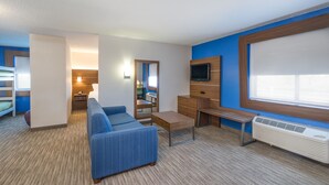 Quarto de hotel moderno com sofá azul, escrivaninha de madeira, televisão e uma janela grande.