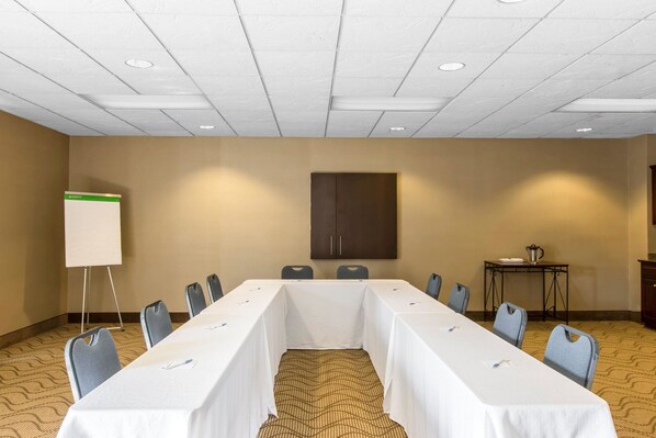 Uma sala de conferência com uma mesa comprida, cadeiras, um quadro branco e um armário.