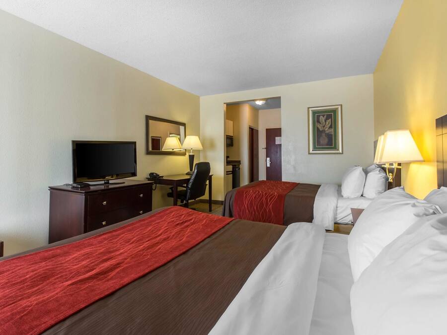 Quarto de hotel com duas camas, uma escrivaninha com televisão e duas luminárias.