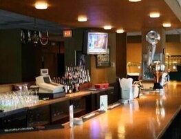 Uma área de bar com balcão, copos e uma tela de televisão.