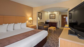 Quarto de hotel com uma cama grande, uma escrivaninha com televisão, uma cadeira, uma mesinha e uma área de kitchenette.