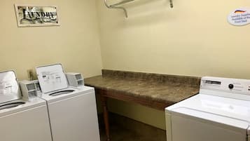 Uma lavanderia com duas máquinas de lavar de abertura frontal, um varal e um aviso indicando lavanderia assistida na recepção.