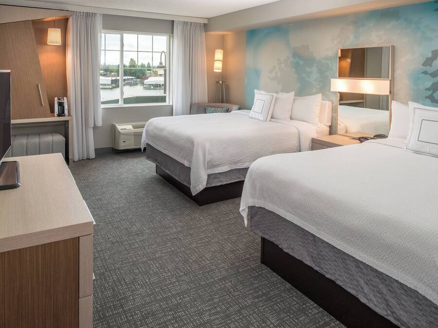 Quarto de hotel com duas camas, uma escrivaninha, televisão e janela com cortinas.