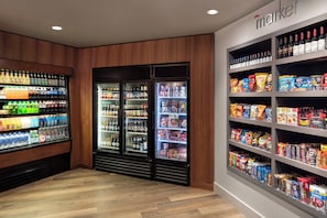 Interior de um supermercado com seções refrigeradas, prateleiras repletas de lanches e diversas bebidas.