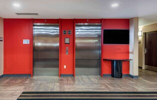 Área de elevadores com paredes vermelhas, duas elevadoras e um cesto de lixo.