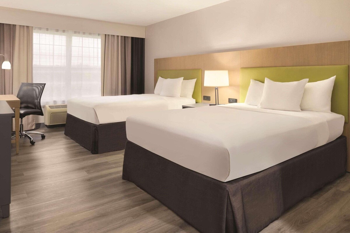 Quarto de hotel com duas camas, uma escrivaninha e uma cadeira.