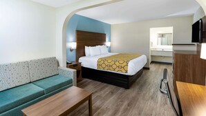 Quarto de hotel com cama, sofá, mesa de madeira, televisão e banheiro com espelho.