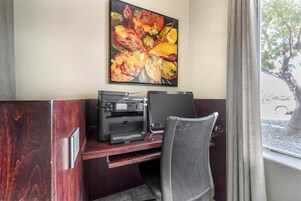 Quarto de hotel com uma secretária de madeira, uma impressora, uma cadeira e uma grande pintura floral na parede.