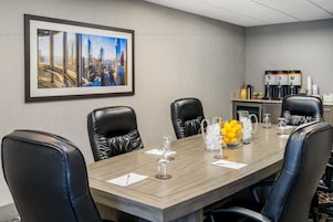 Uma sala de conferências com uma pintura de paisagem urbana, um espaço para café e uma mesa com cadeiras e um vaso de limões.