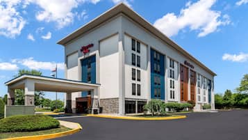Um hotel Hampton Inn com entrada coberta, vários andares e céu claro.
