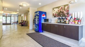 Uma área de recepção com máquina de refrigerantes Pepsi, um espaço com café e uma obra de arte na parede.