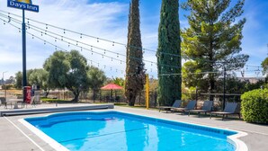 Uma piscina com a placa Days Inn, rodeada por árvores altas e uma área cercada com espreguiçadeiras.