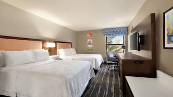 Quarto de hotel com duas camas, uma escrivaninha, uma cadeira, uma televisão e janela com vista.