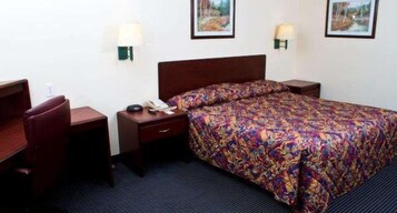 Quarto de hotel com cama, escrivaninha, cadeira, mesa de cabeceira e duas luminárias de parede.