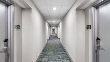 Corredor de hotel com piso em carpete, paredes brancas e portas em ambos os lados.