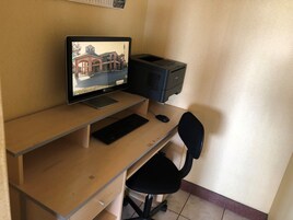 Uma escrivaninha com um computador de mesa, impressora, teclado, rato e uma cadeira de escritório preta.