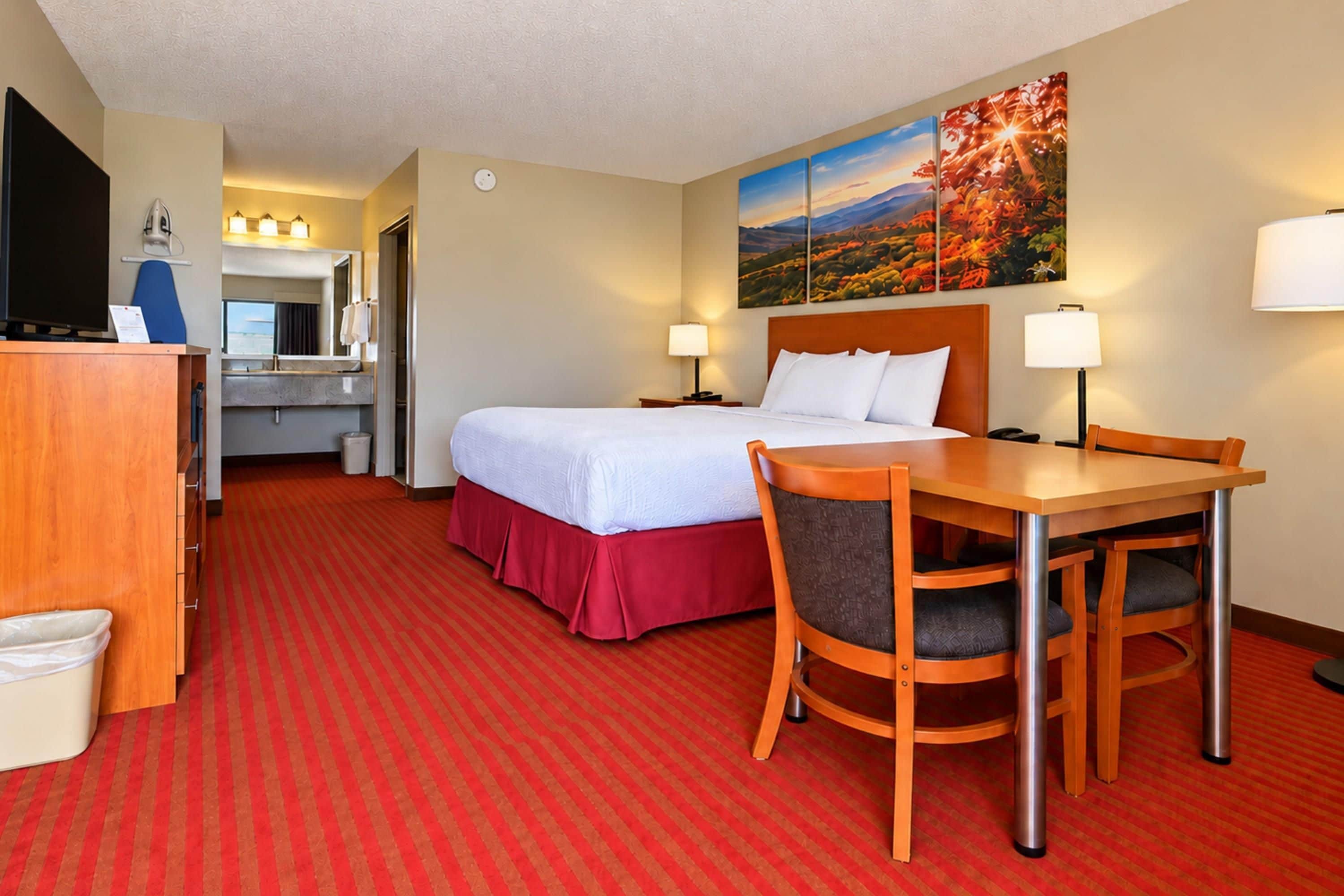 Quarto de hotel com cama, escrivaninha, cadeira e um quadro na parede.