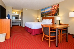 Quarto de hotel com cama, escrivaninha, cadeira e um quadro na parede.