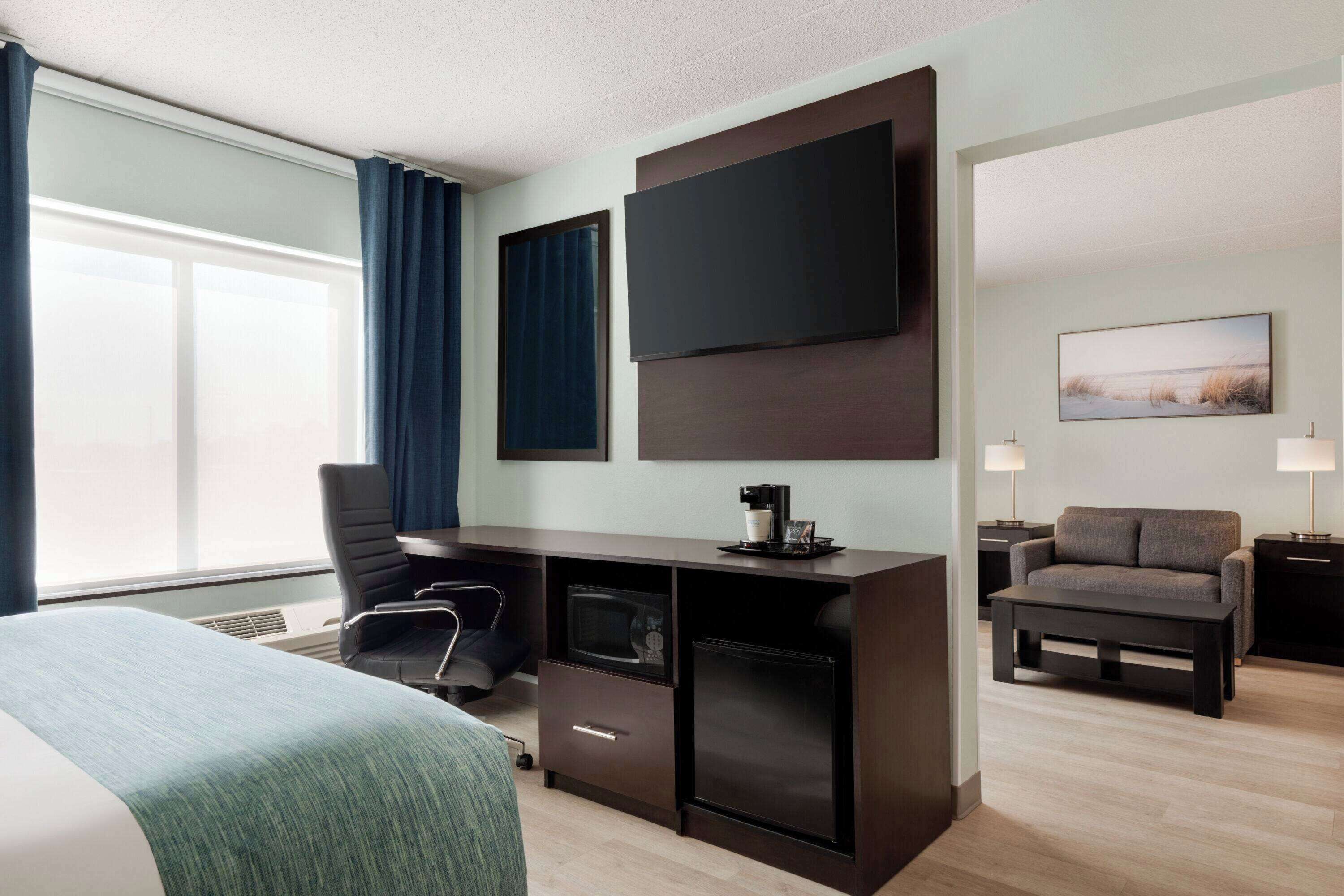 Quarto de hotel com cama, escrivaninha, cadeira, televisão e sofá.