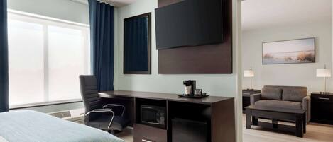 Quarto de hotel com cama, escrivaninha, cadeira, televisão e sofá.