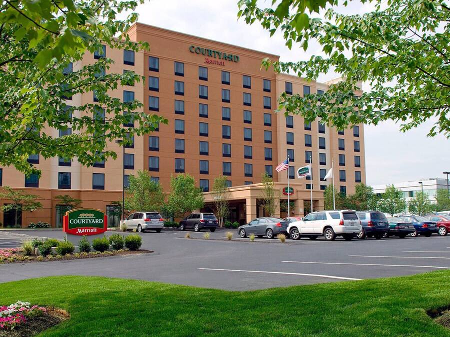 Um hotel Courtyard Marriott com estacionamento, vários carros e vegetação ao redor.