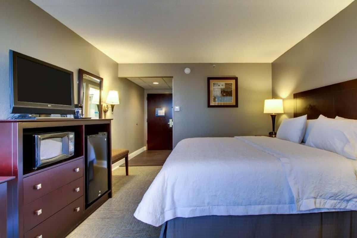 Quarto de hotel com uma cama, televisão, micro-ondas, secretária com gavetas e porta que dá para outro espaço.
