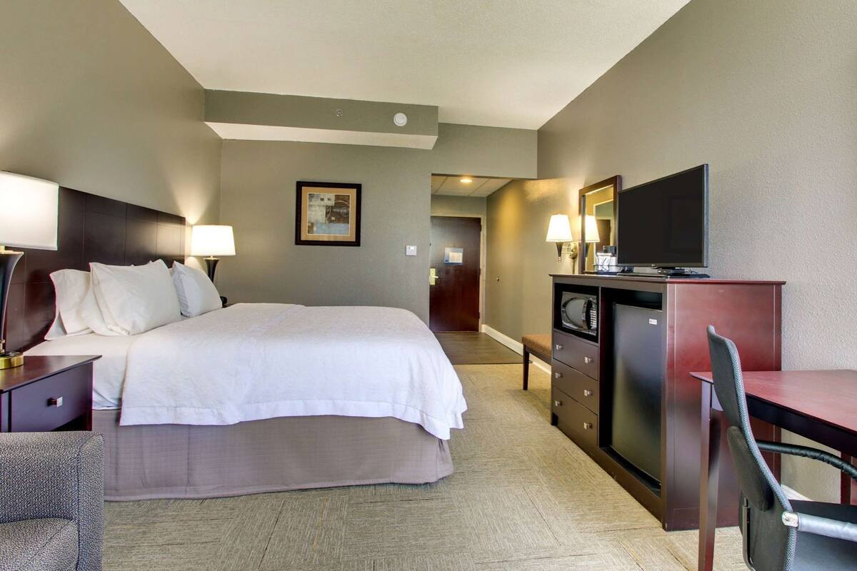 Quarto de hotel com cama, mesas de cabeceira, escrivaninha com cadeira, televisão e micro-ondas.