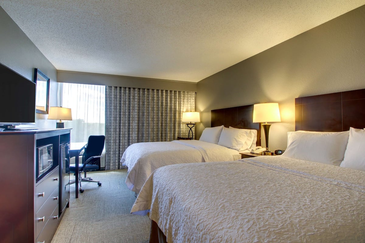 Quarto de hotel com duas camas, uma escrivaninha, uma cadeira e uma televisão.