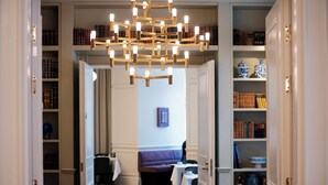 Um corredor com um candelabro, estantes de livros, um sofá roxo e uma área de jantar.