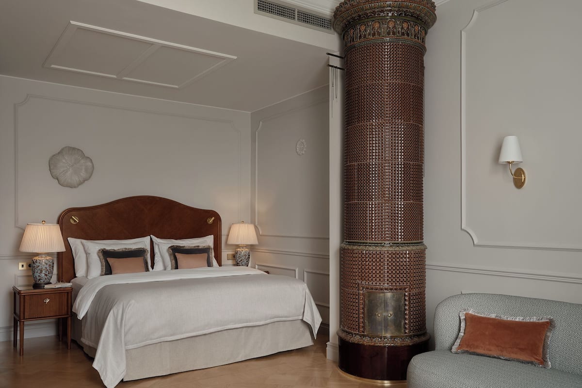 Quarto com cama grande, duas mesas de cabeceira com luminárias, um pilar decorativo e um sofá.