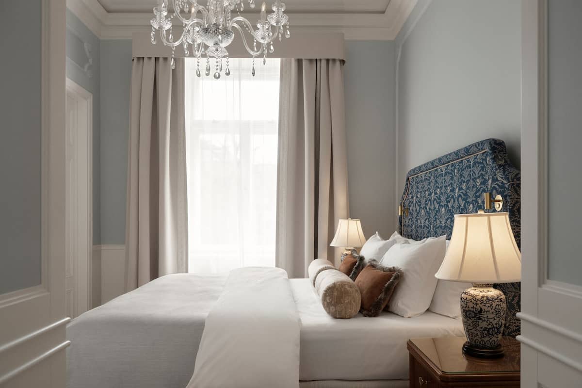 Um quarto bem arrumado com uma cama grande, um candelabro, um painel de cabeceira estampado e duas luminárias de mesa.