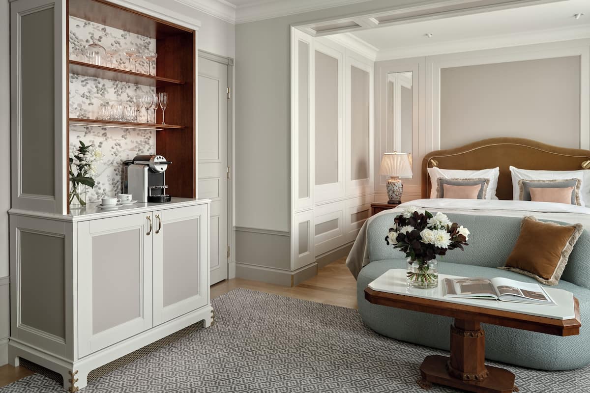 Quarto de hotel com um armário grande, uma cama com almofadas, uma mesinha de cabeceira com um livro e uma máquina de café.