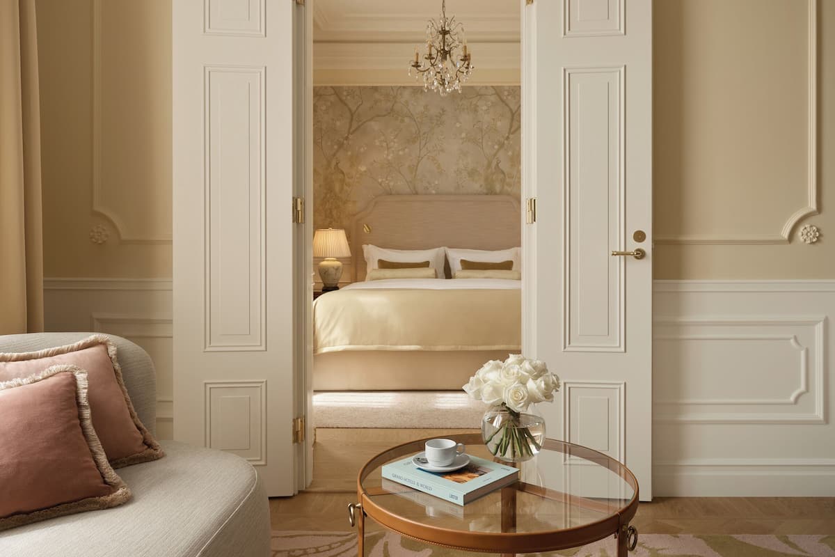 Quarto de hotel com cama, área de estar com mesinha de café e lustre.