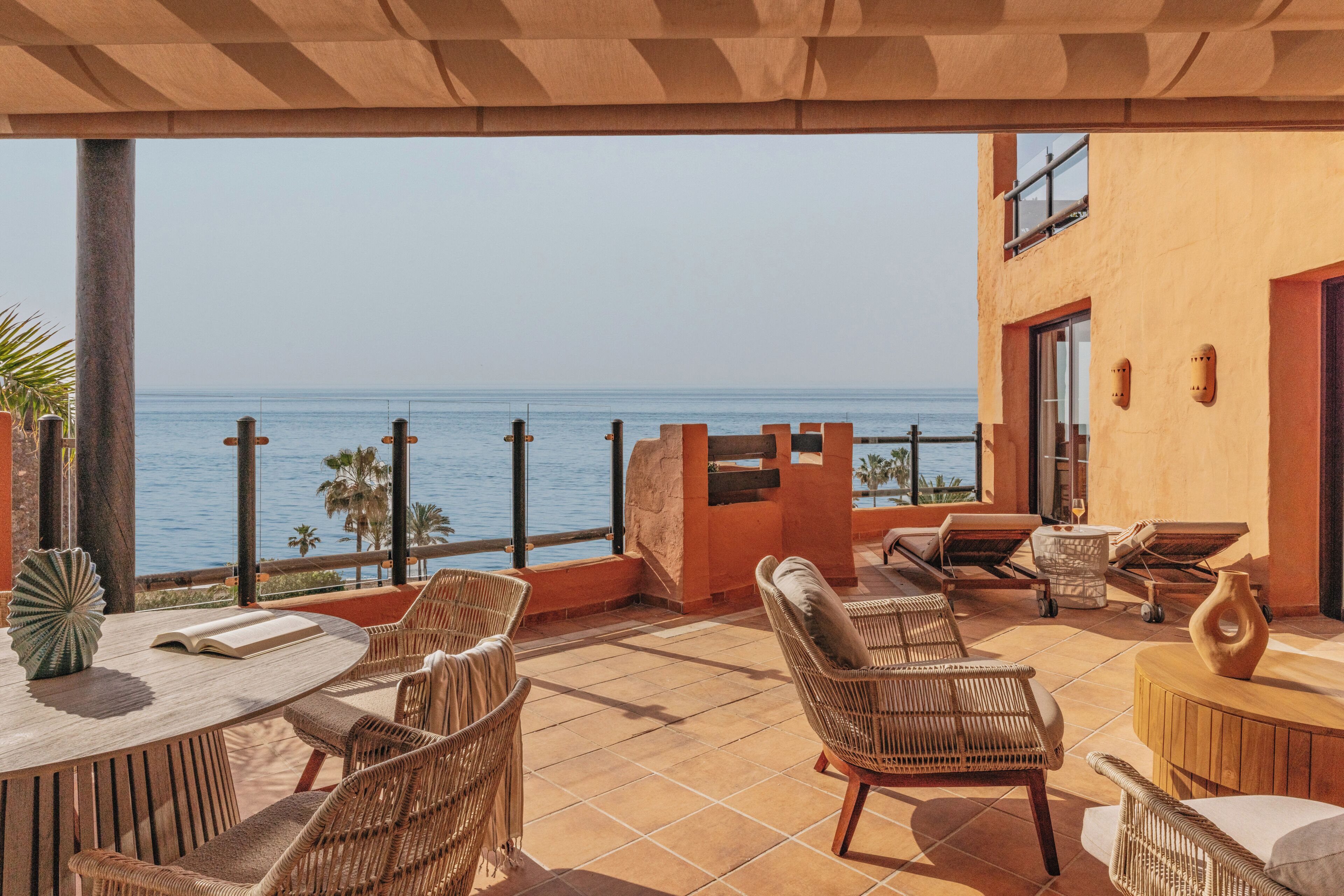 Um terraço com mobiliário de vime, uma mesa e vista para o mar.
