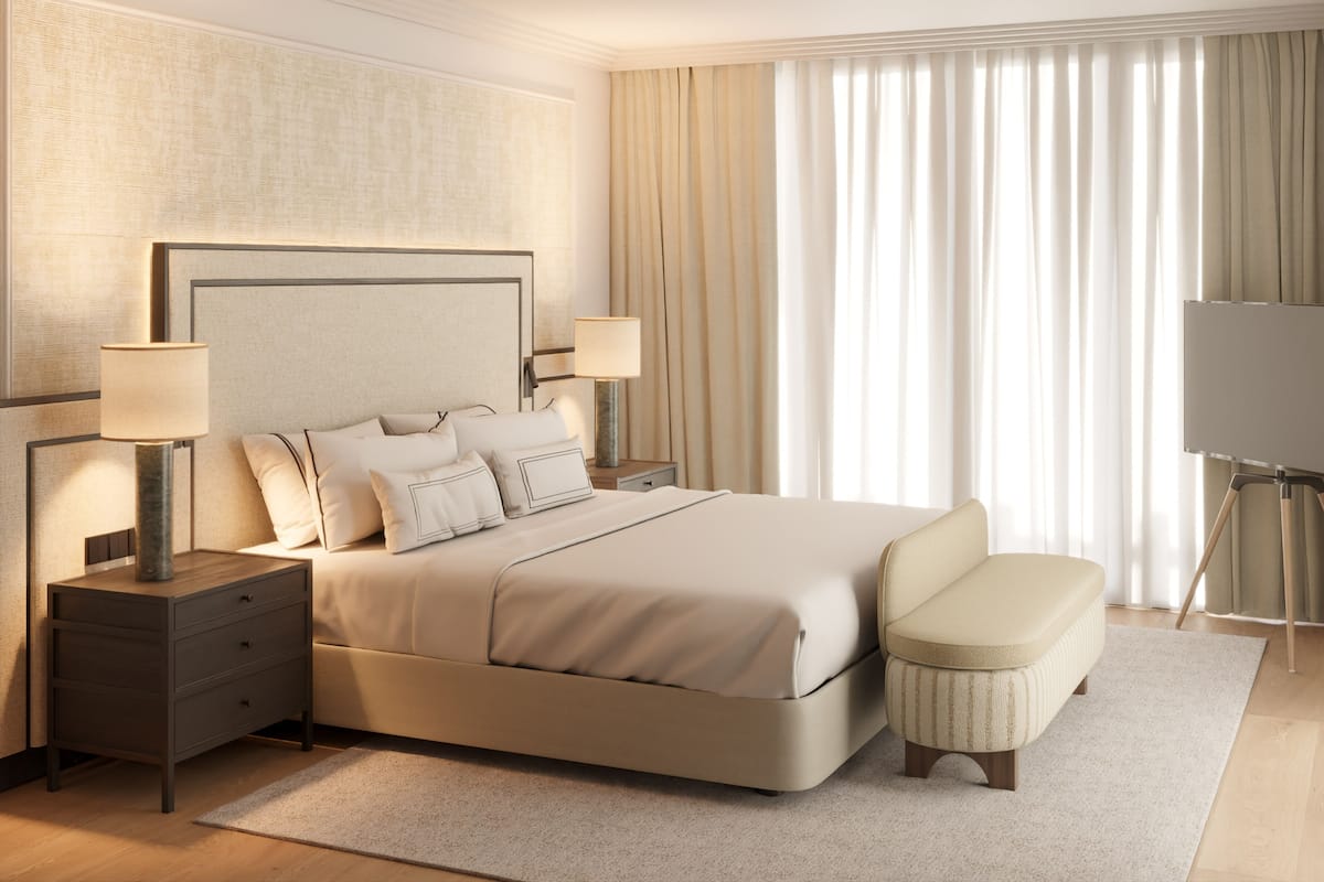 Quarto de hotel moderno com uma cama grande, luminárias de cabeceira, uma mesinha, um banco e uma TV em um suporte.