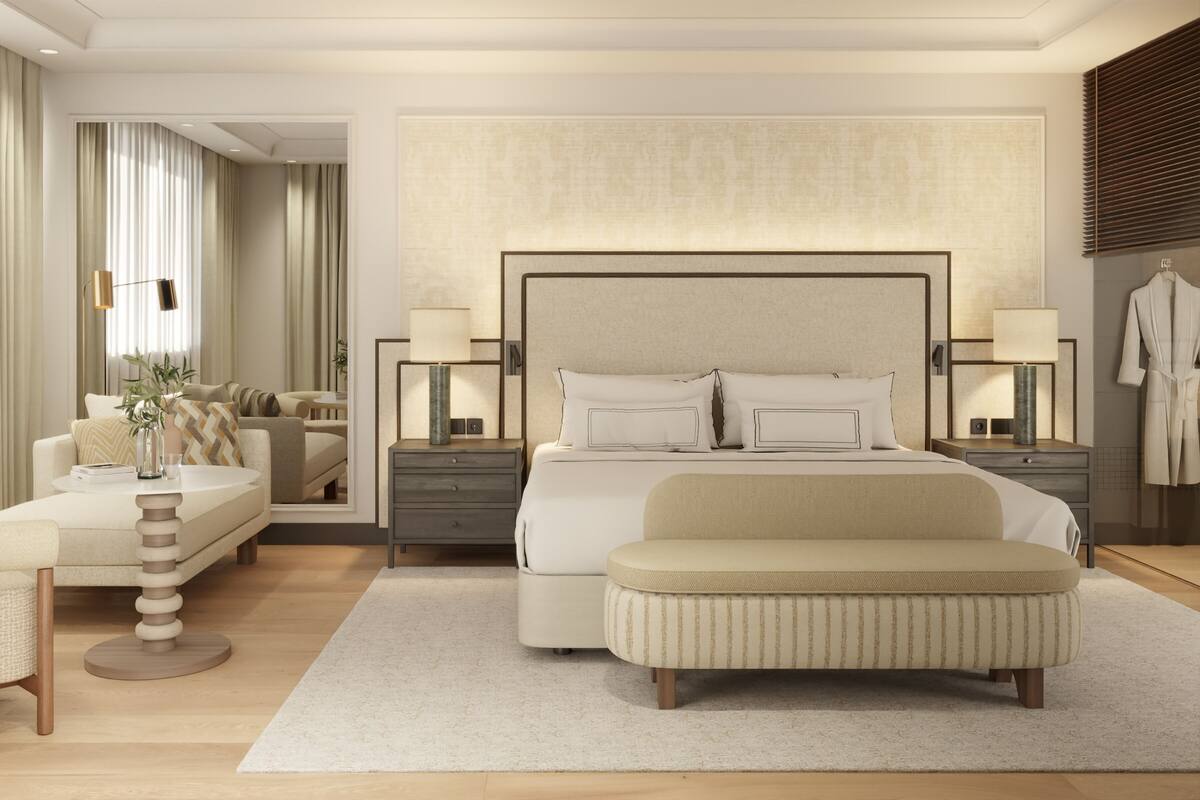 Quarto de hotel moderno com uma cama grande, mesas de cabeceira, um sofá, uma cadeira e um espelho.