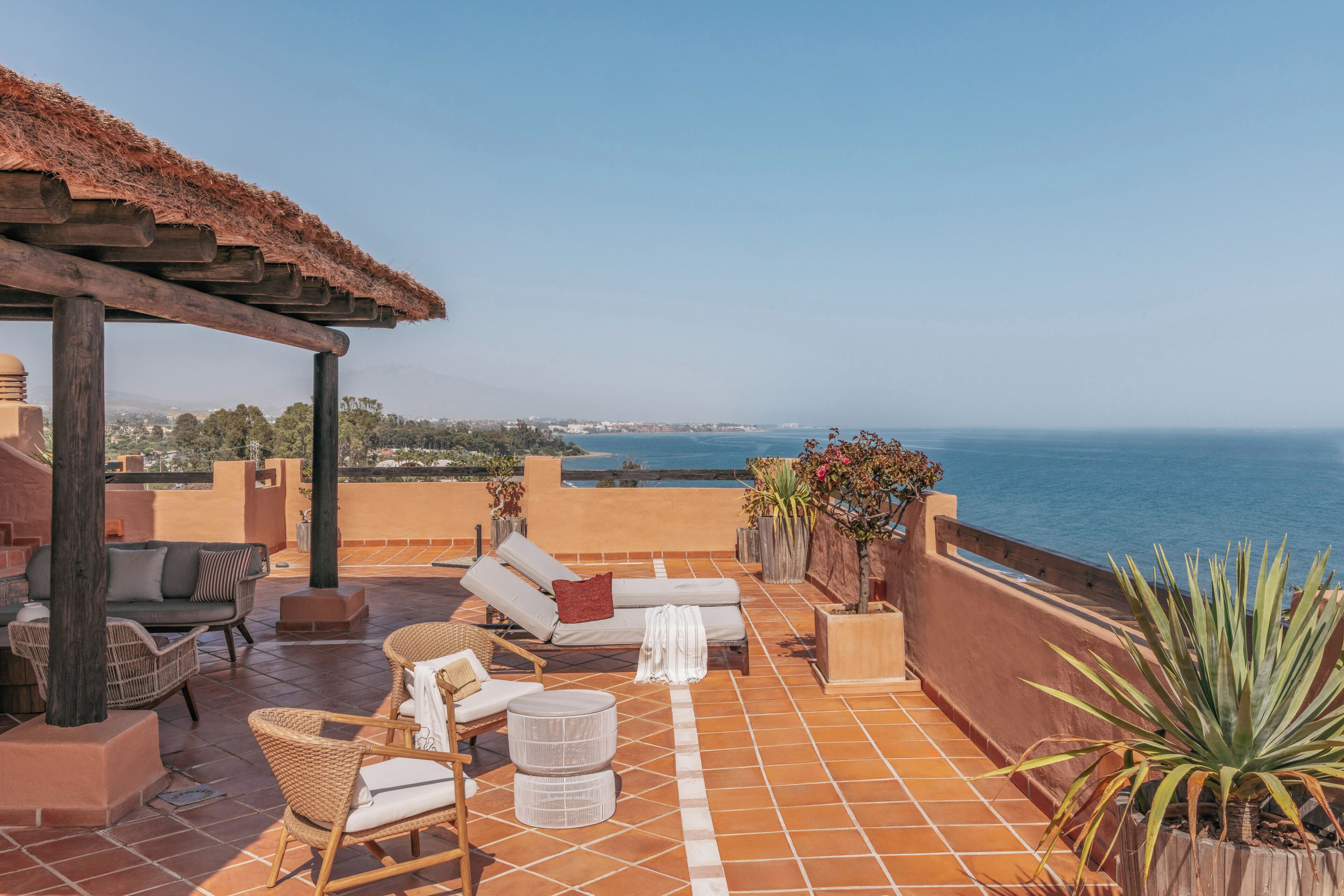 Um terraço com mobiliário ao ar livre, uma pérgula e vista para o mar.