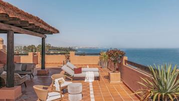 Um terraço com mobiliário ao ar livre, uma pérgula e vista para o mar.