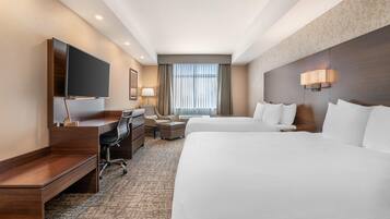 Quarto de hotel com uma cama grande, uma escrivaninha com cadeira, uma televisão e uma janela com cortinas.