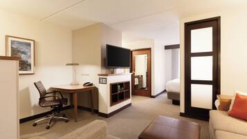 Quarto de hotel com escrivaninha, cadeira, televisão, sofá e apoio para os pés.